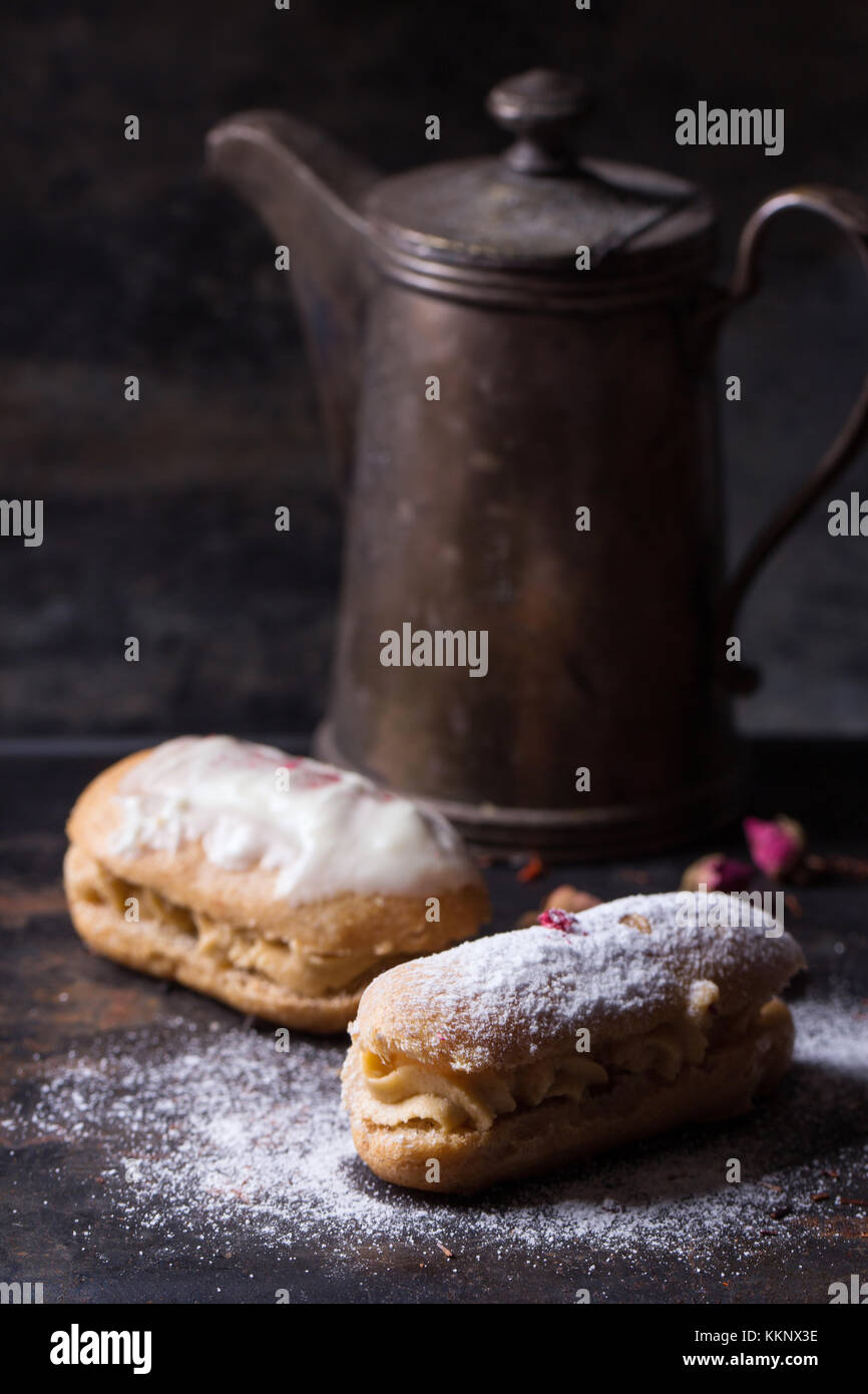 Two eclairs with white chocolate and vintage teapot over dark ...