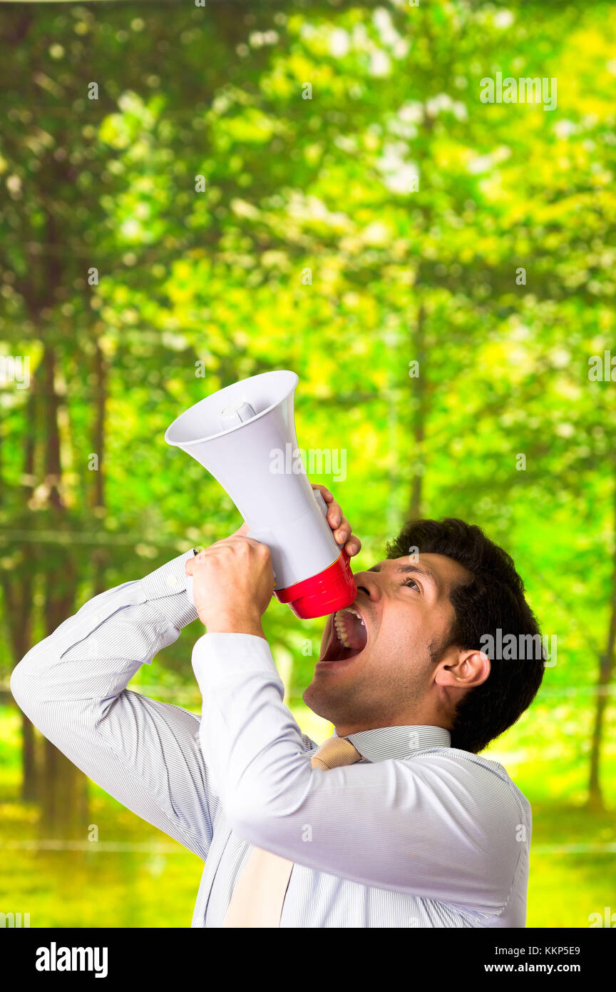 Portrait of a handsome man shouting with a megaphone in a blurred green ...