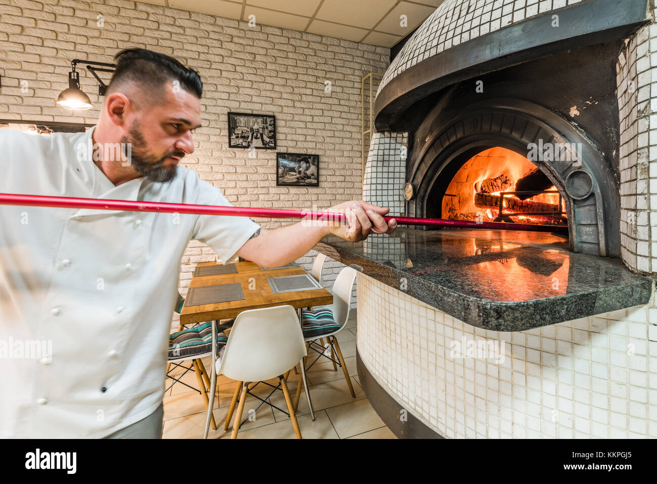 Handsome pizzaiolo man baking pizza in woodfired oven in local pizzeria ...