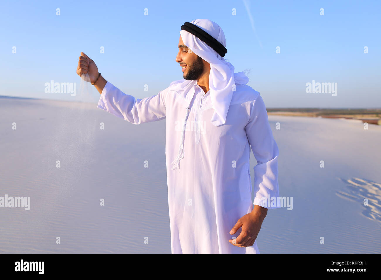 Young Arab guy who takes sand in hand and lifts it to smiling face and ...