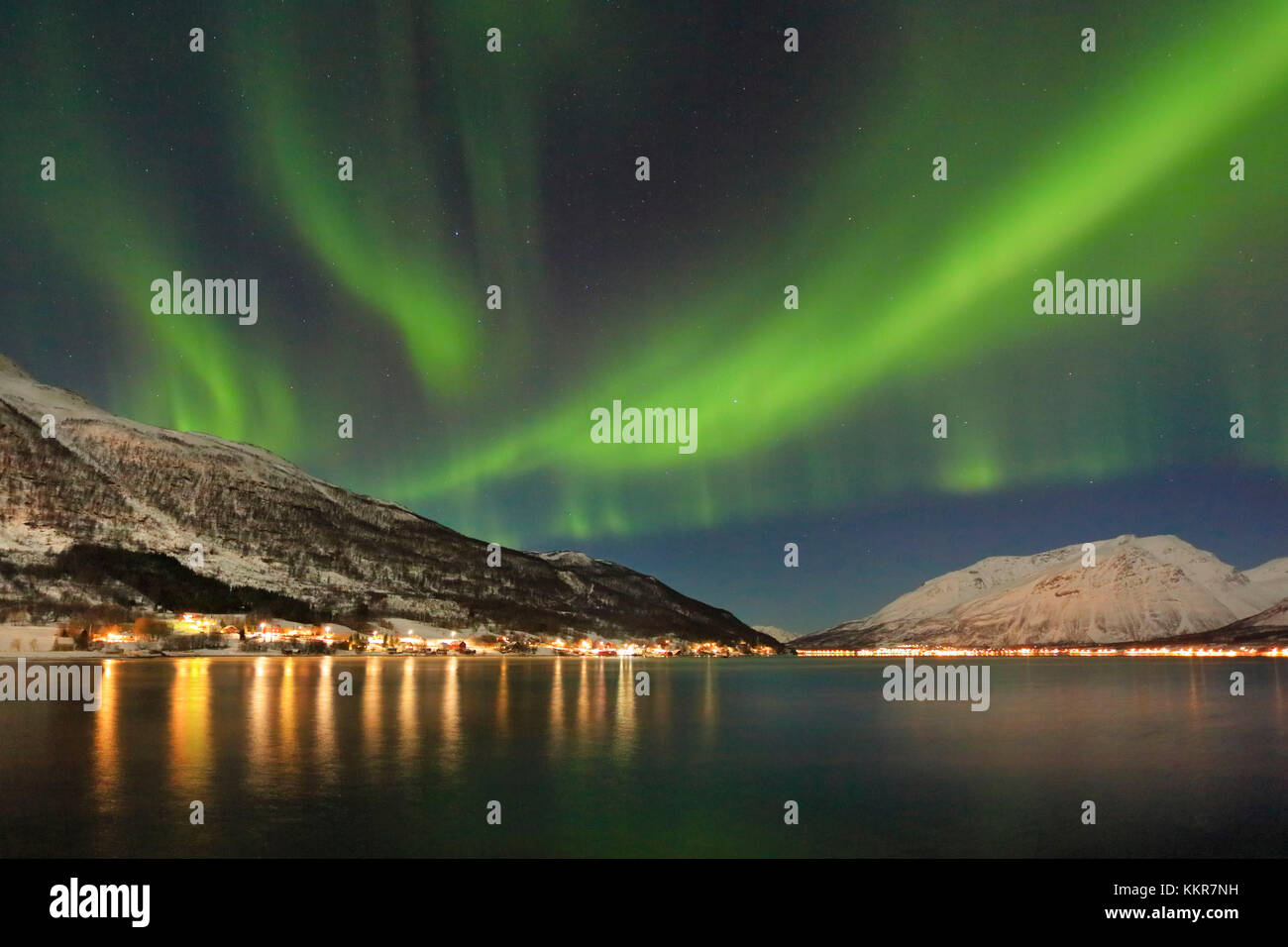 The Northern Lights is reflected in the icy sea surrounded by snowy ...