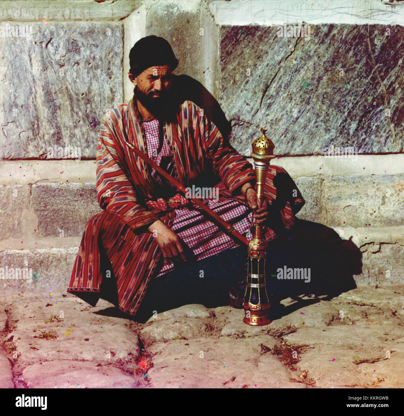 This image shows a man sitting and holding a hookah, commonly used in ...