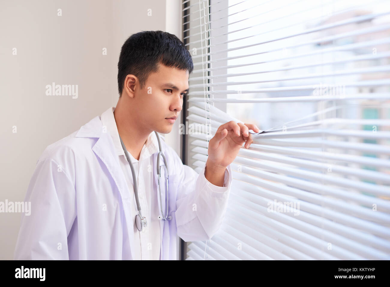 Young male asian doctor looking out of the window at hospital Stock ...