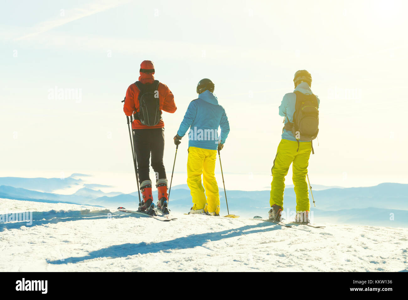 Three skiers preparing for a downhill ride from the very top of a ...