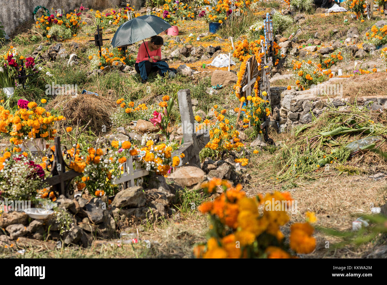 A woman sits by the grave of a relative surrounded by marigold ...