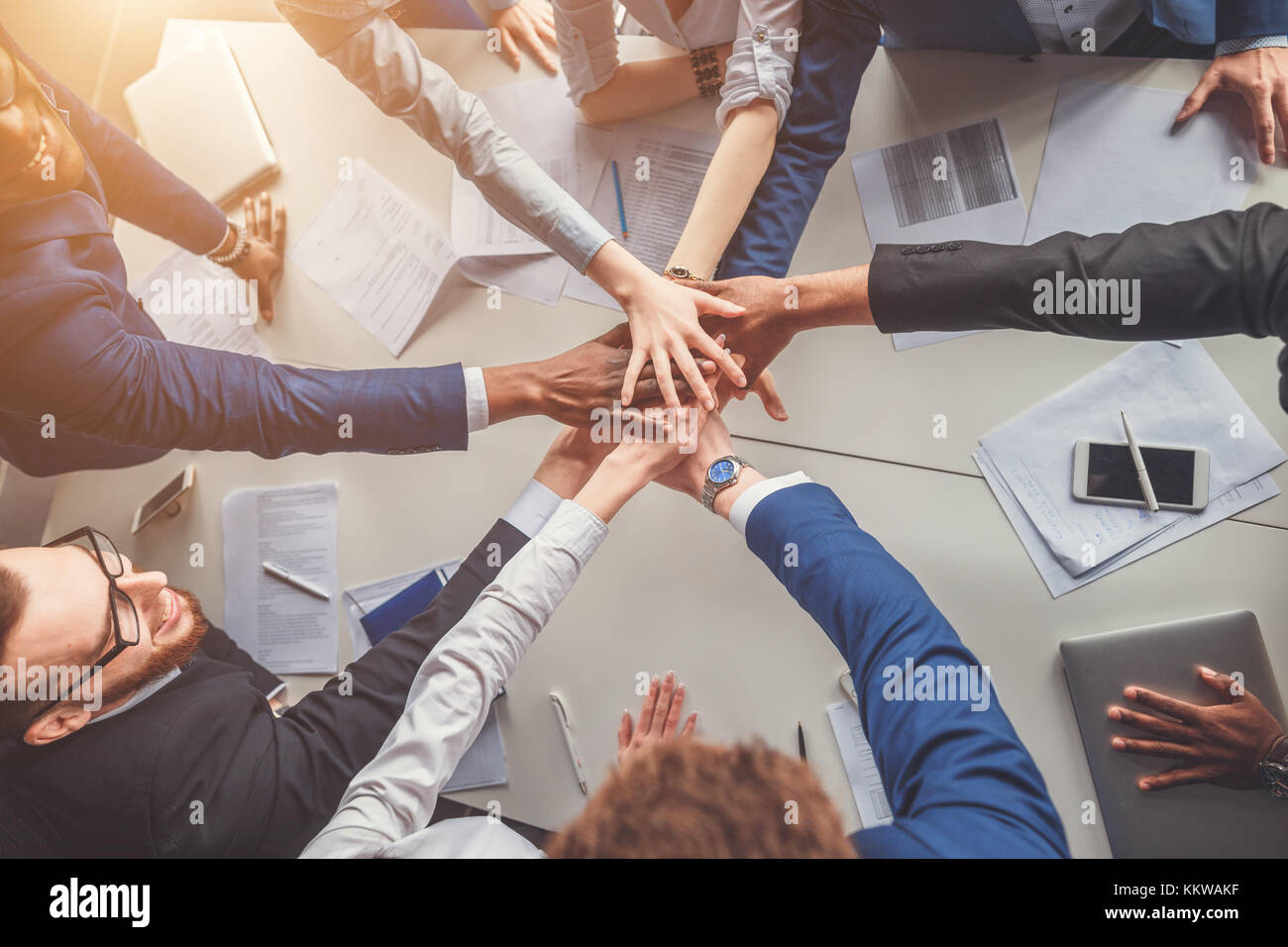Close-up of people holding hands together while sitting around the desk ...
