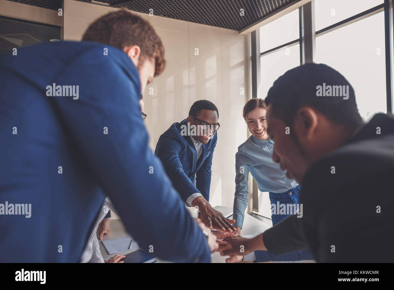 Close-up of people holding hands together while sitting around the desk ...