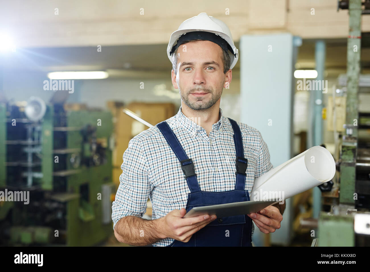Engineer in uniform and helmet holding rolled blueprint and touchpad ...