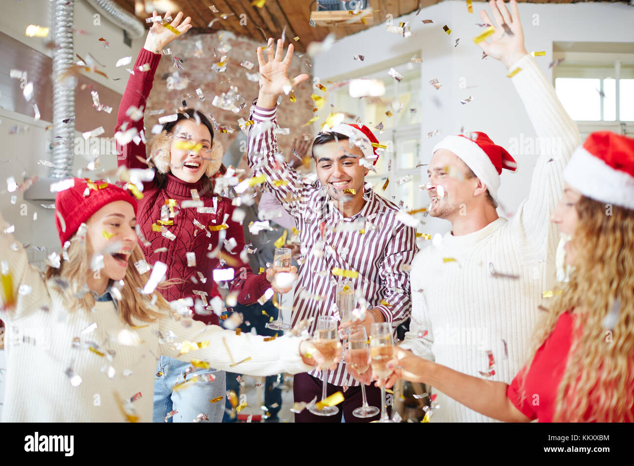 Guys and girls cheering up with champagne while enjoying confetti fall ...