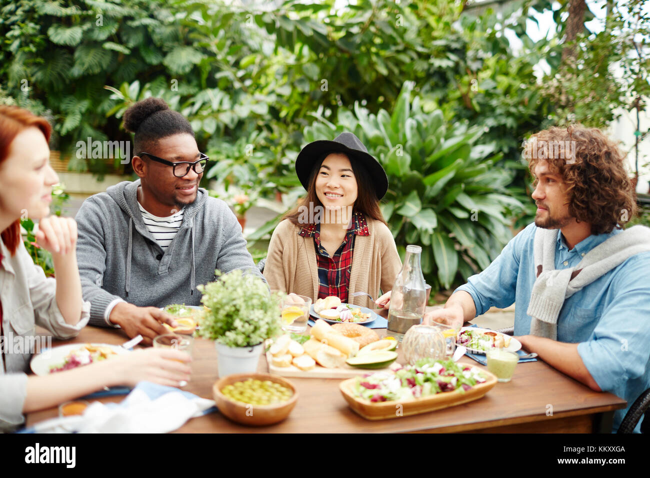 Group of young intercultural friends having talk by served table at ...