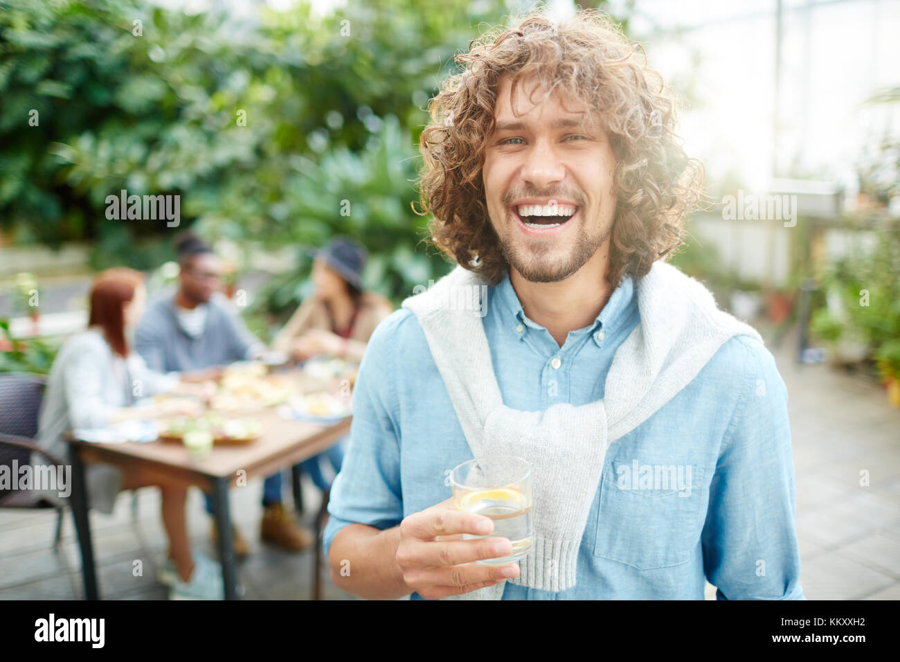 Laughing guy with drink looking at camera while his friends having ...