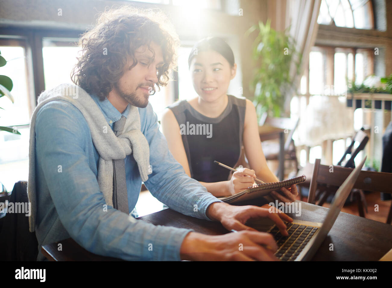 Young businessman typing while listening to Asian colleagues sharing ...
