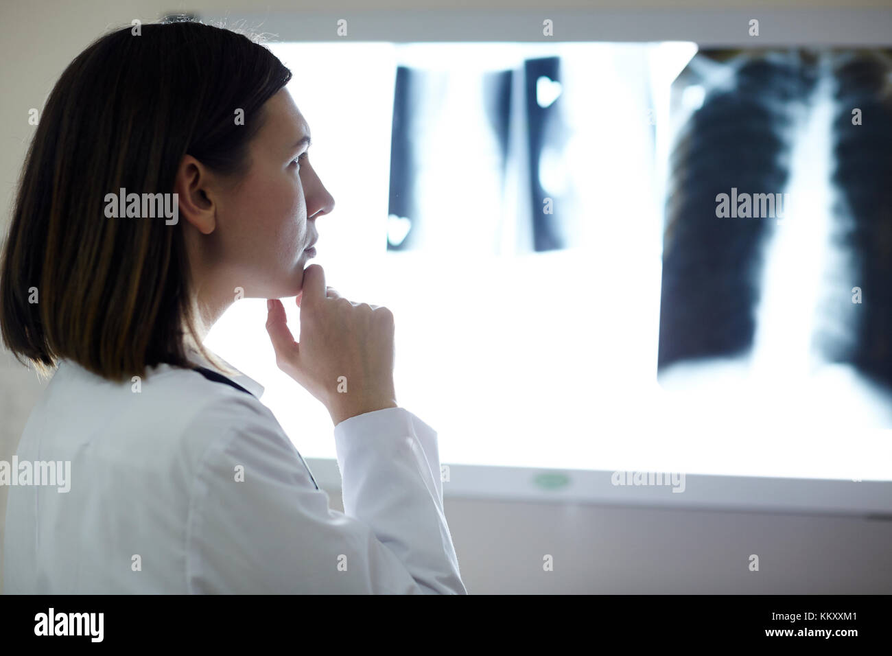 Pensive radiologist looking attentively at one of x-ray images in lab ...
