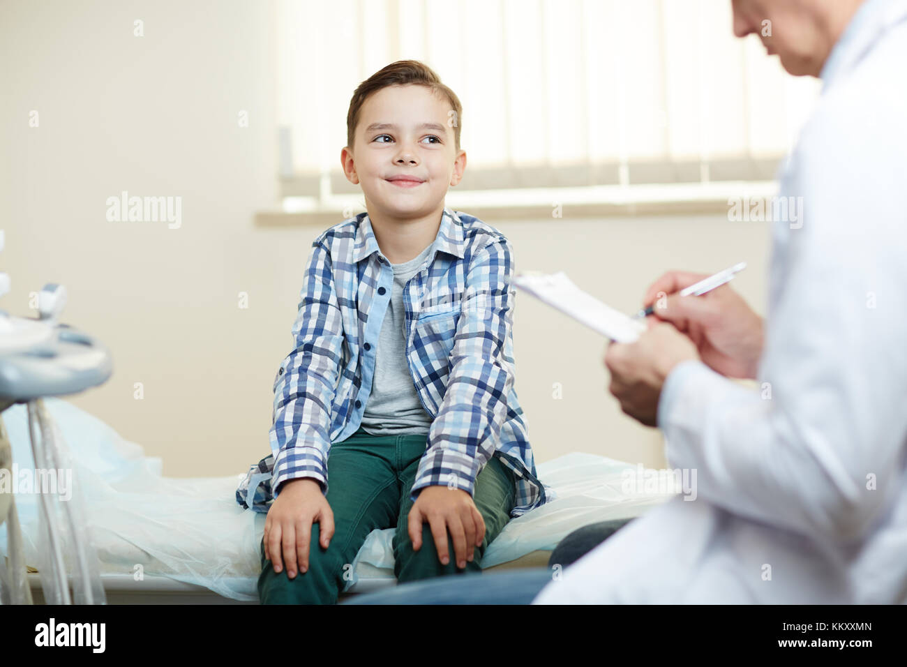 Happy little boy looking at his doctor while he making prescriptions ...