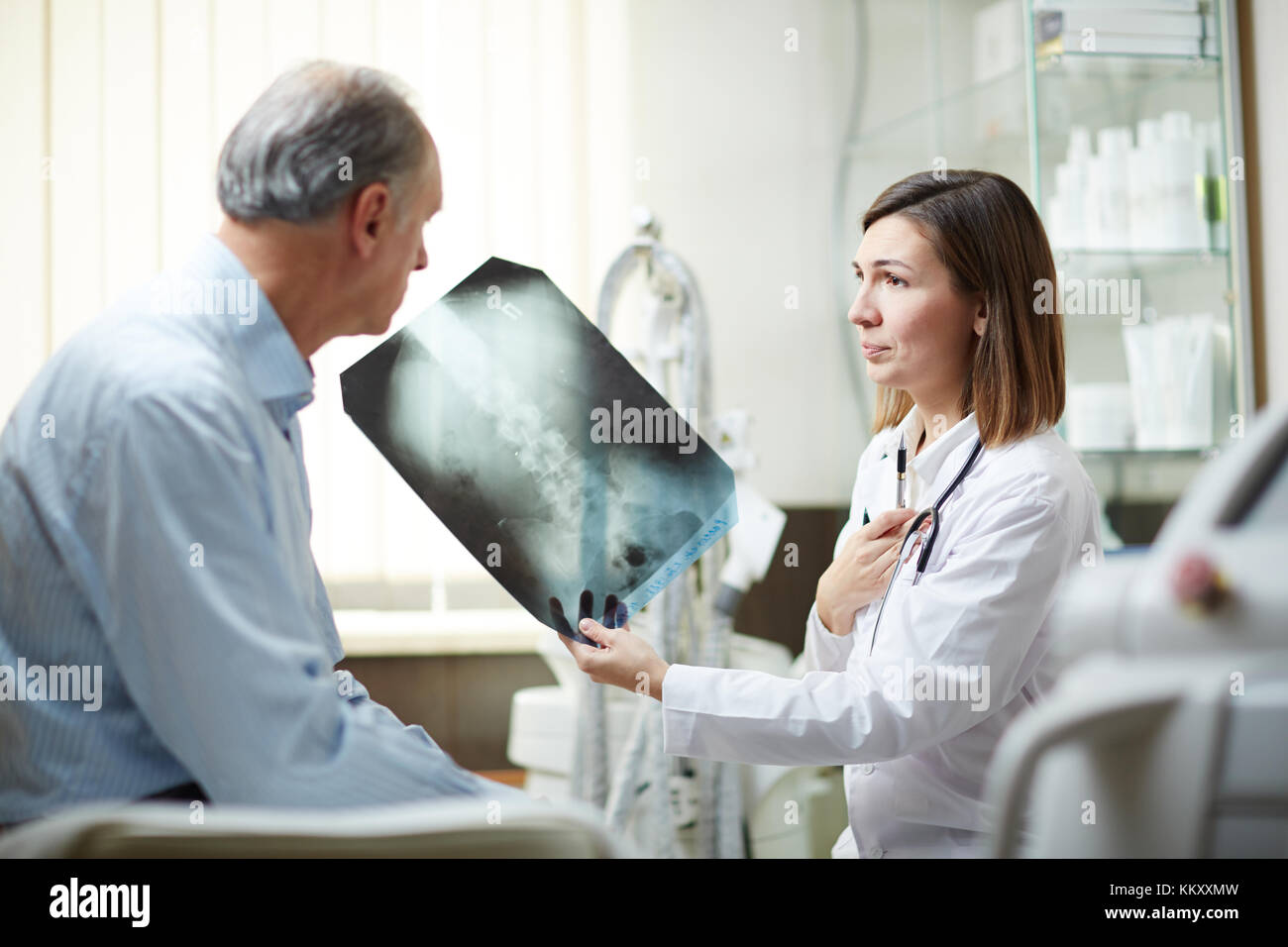 Young radiologist showing x-ray image to her aged patient and giving ...