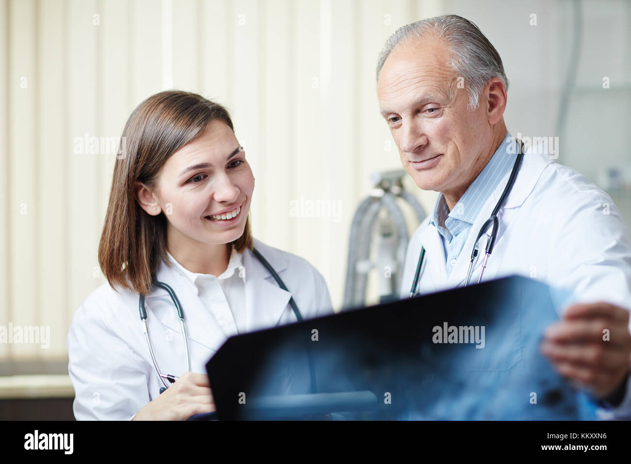 Smiling medical staff in uniform looking at x-ray of spinal cord in ...