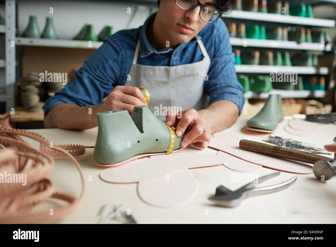 Contemporary cobbler measuring boot workpiece on table in his workshop ...