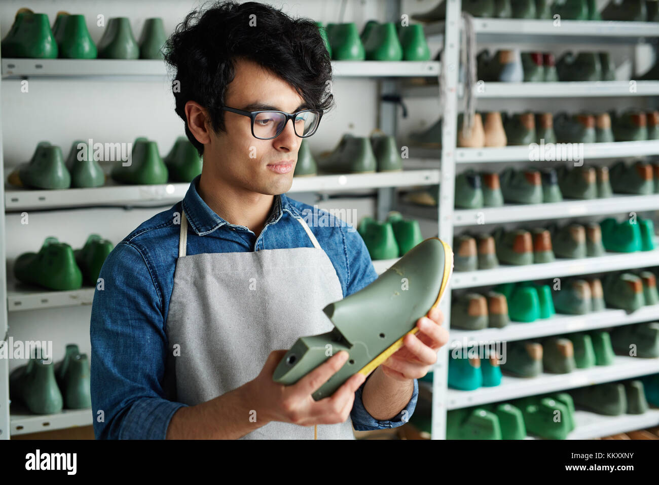 Young shoemaker holding plastic boot workpiece and measuring its sole ...