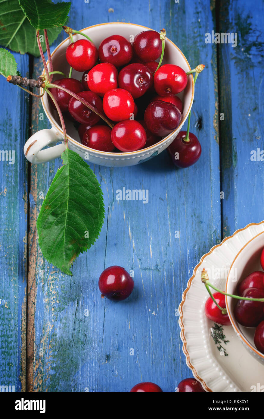 Fresh cherries in vintage tea cups on blue wooden table Stock Photo - Alamy