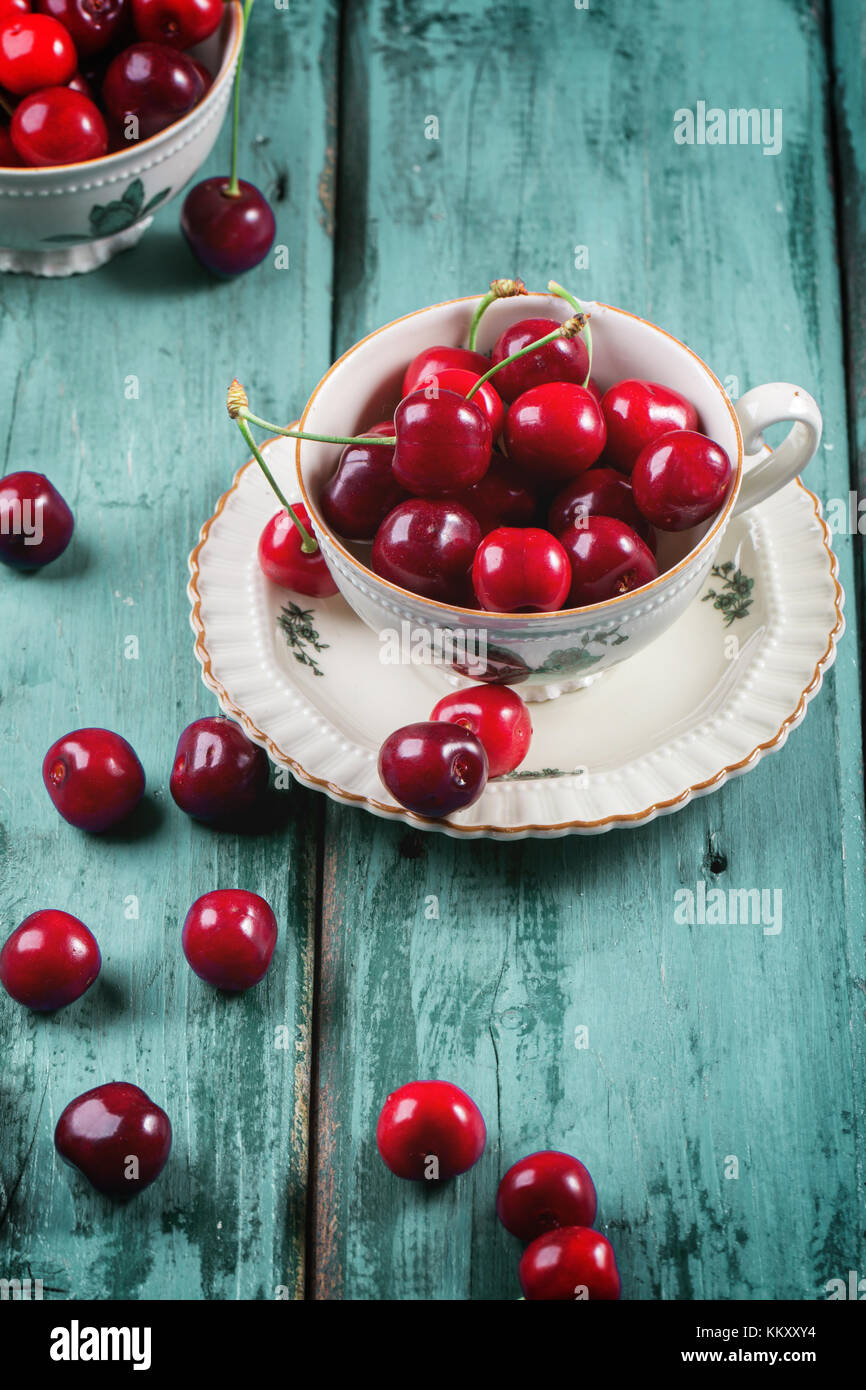 Fresh cherries in vintage tea cups on blue wooden table Stock Photo - Alamy