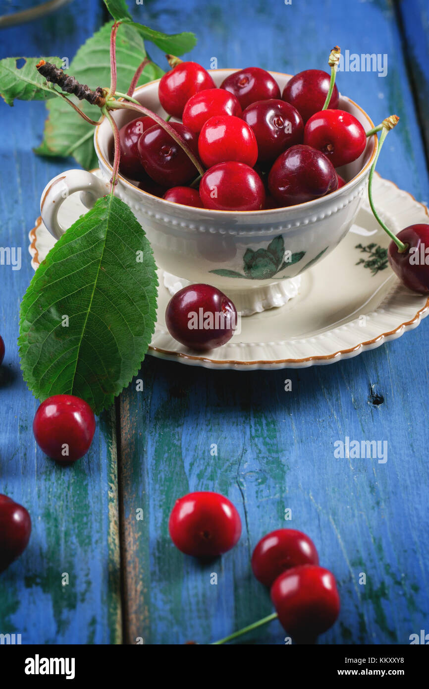 Fresh cherries in vintage tea cups on blue wooden table Stock Photo - Alamy
