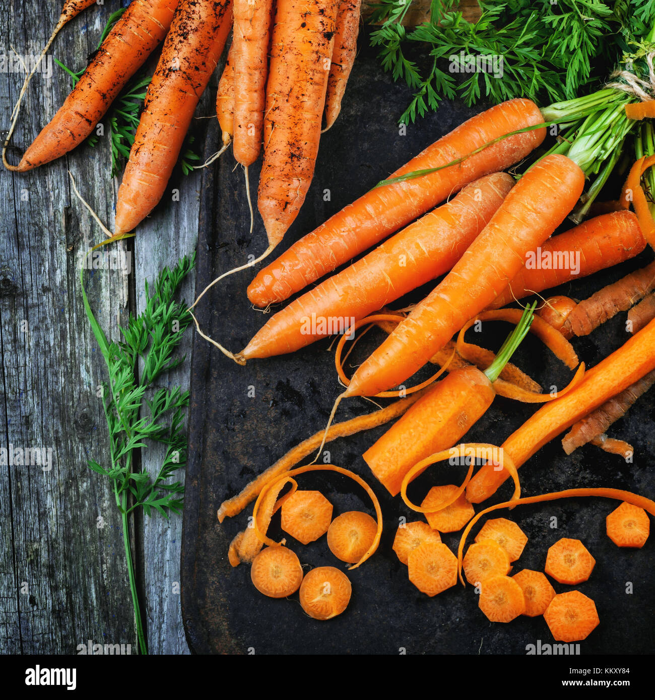 Fresh whole and sliced carrots over black cutting board over wooden ...