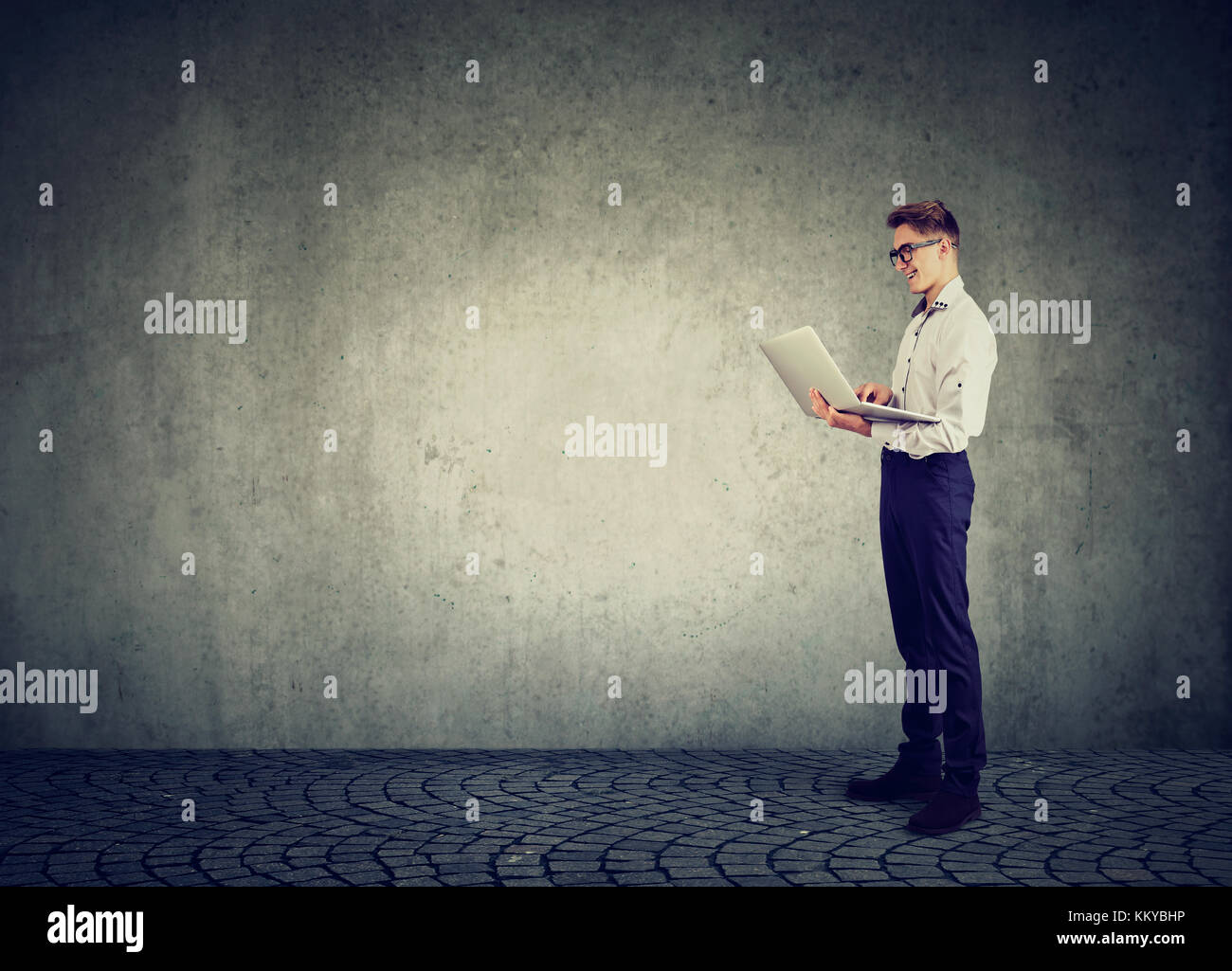 Business man using his laptop computer standing along concrete wall ...