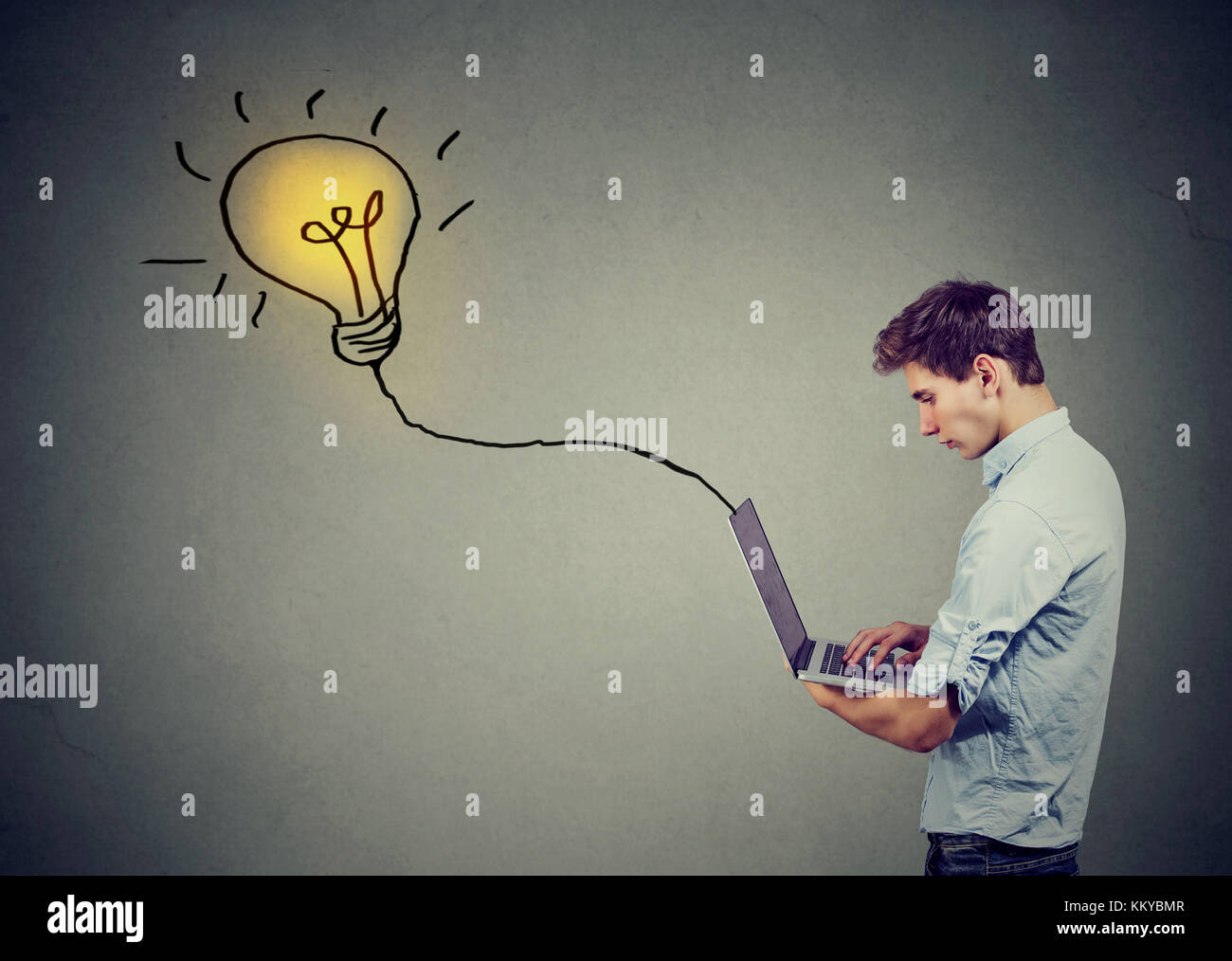 Young man using a laptop with light bulb plugged in it Stock Photo - Alamy