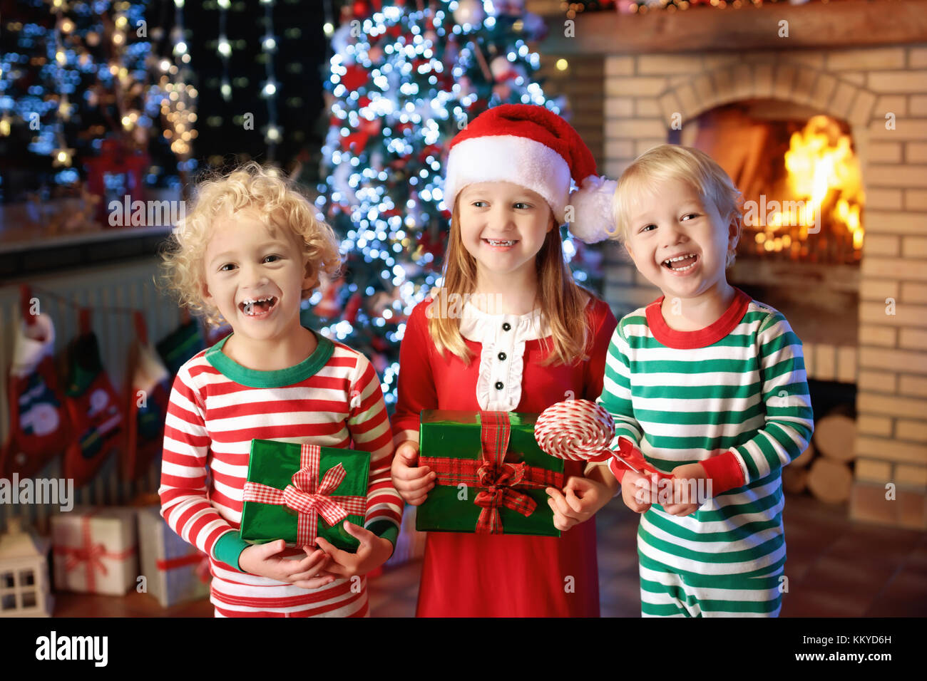 Children at Christmas tree and fireplace on Xmas eve. Family with kids ...