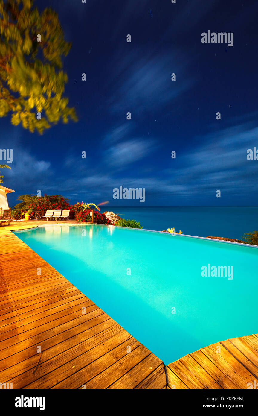 An illuminated hotel pool overlooking the Caribbean Sea at night in ...