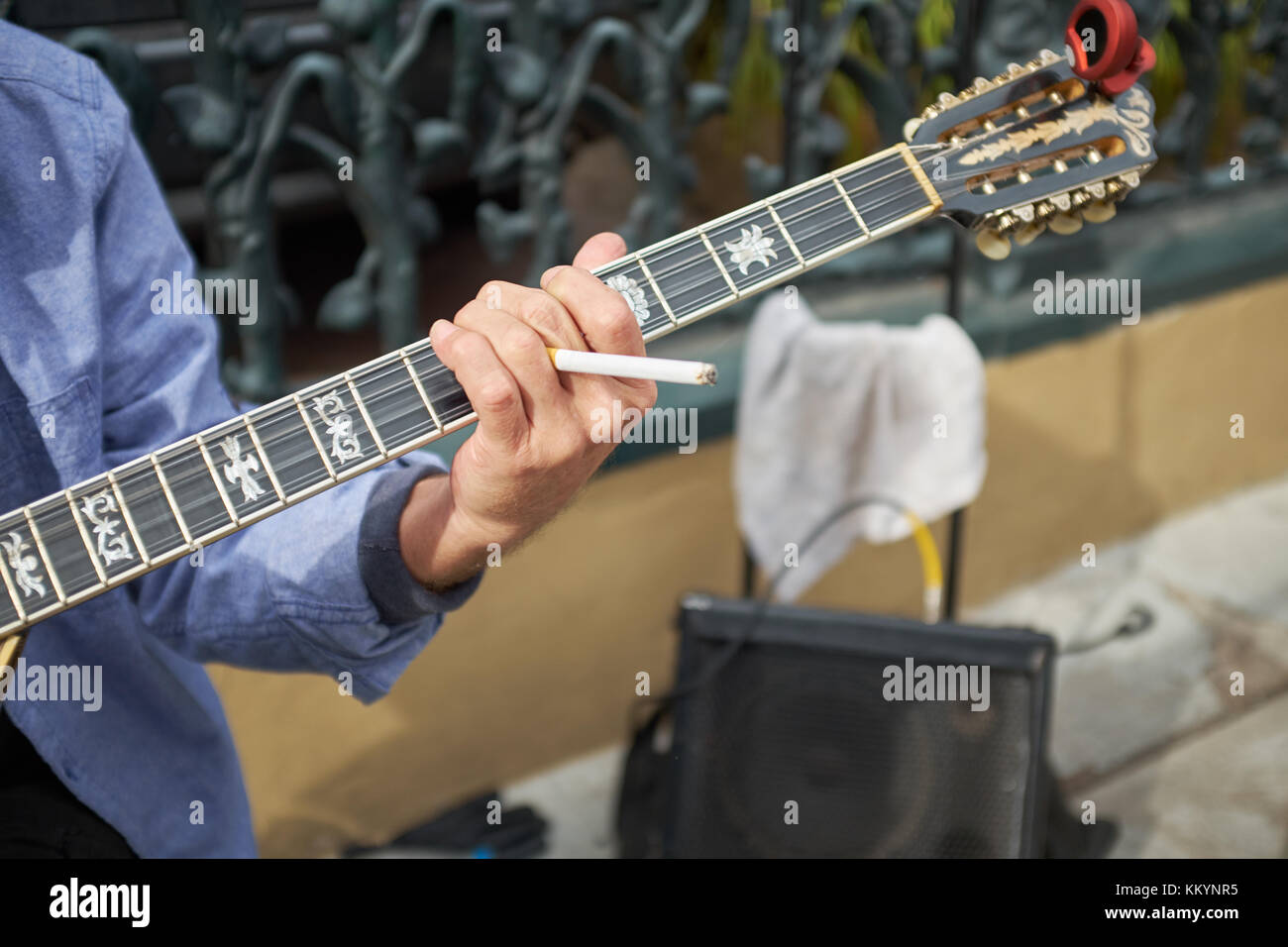 Musician smoking a cigarette playing a guitar outdoors in the street ...