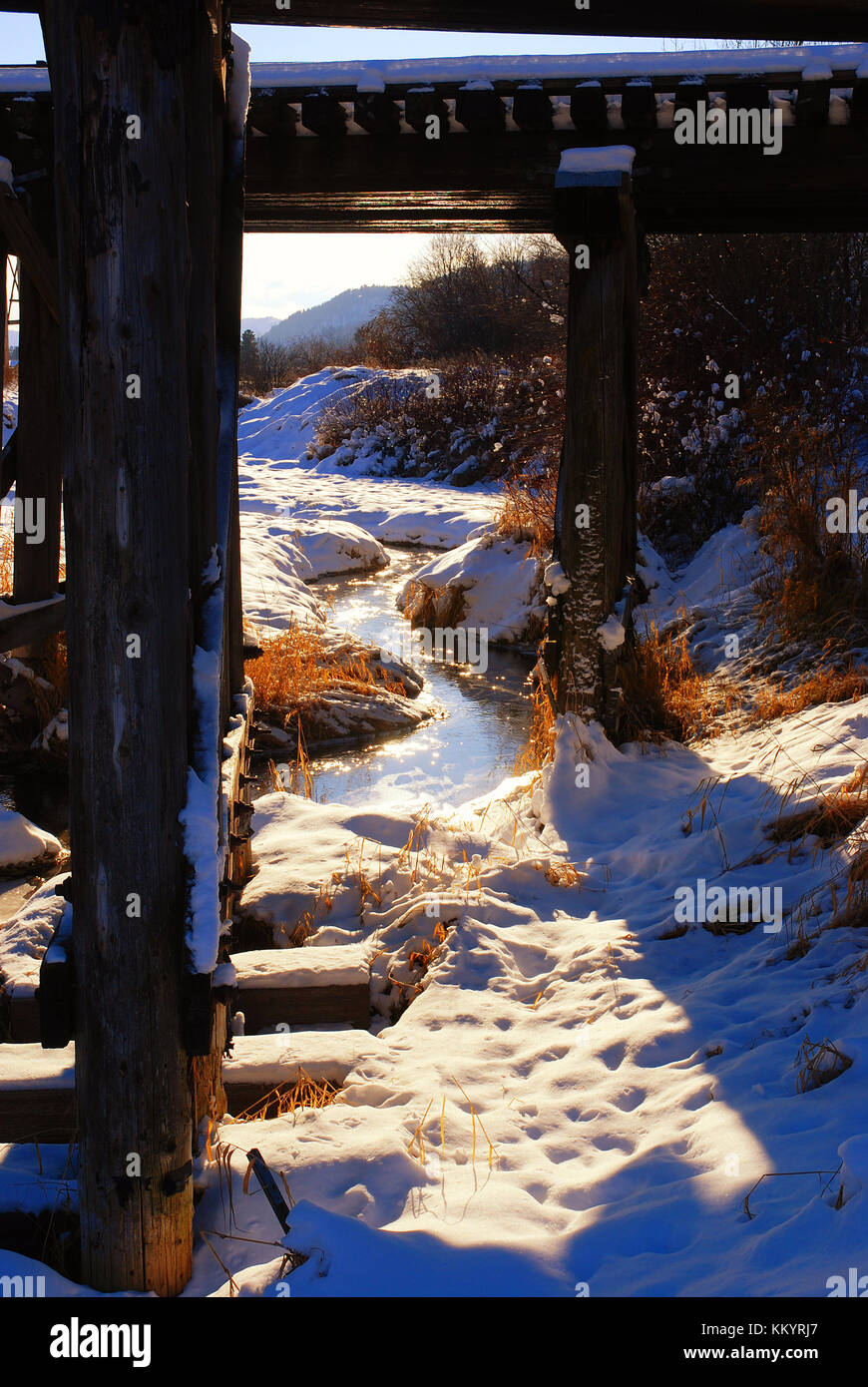 Creek running underneath a wooden train tressel surrounded by snow ...