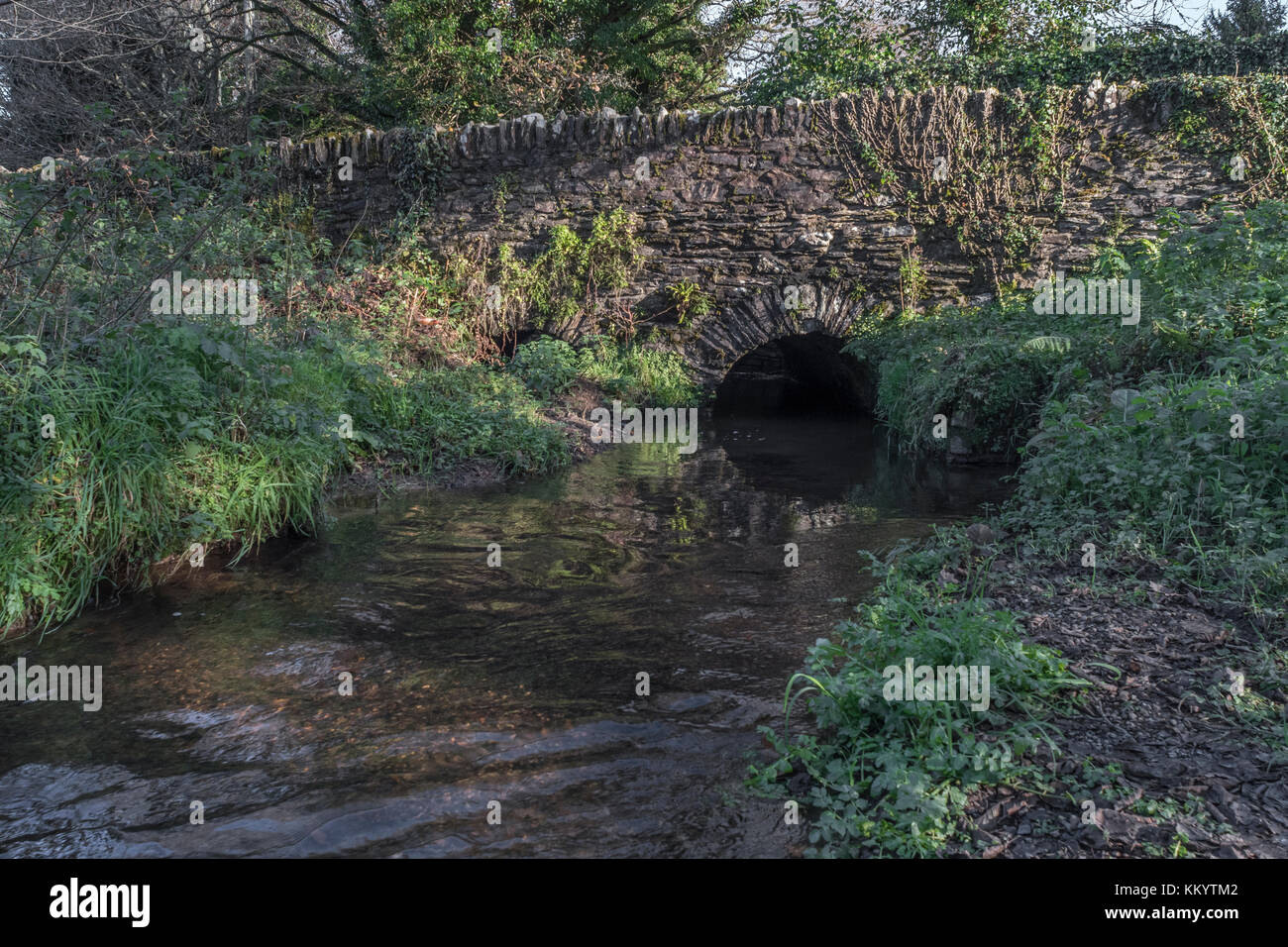 Small rural stone bridge arching over a small, clear-running, stream ...