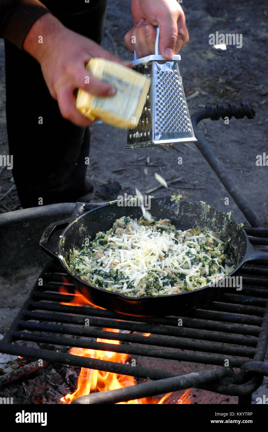 Man grating cheese onto egg scramble in cast iron skillet over a ...