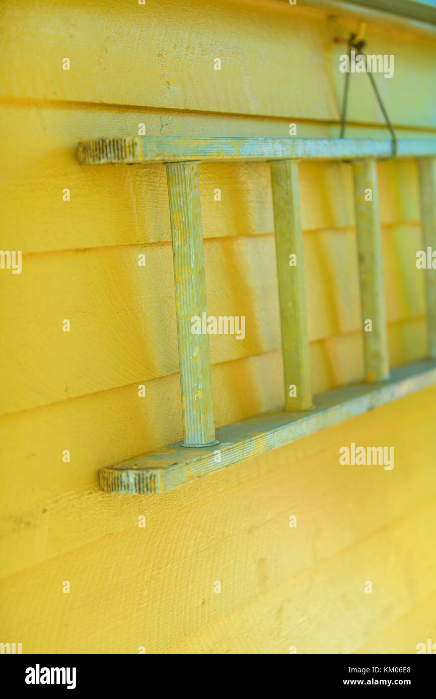 Wooden old ladder hanging on yellow house wall Stock Photo - Alamy