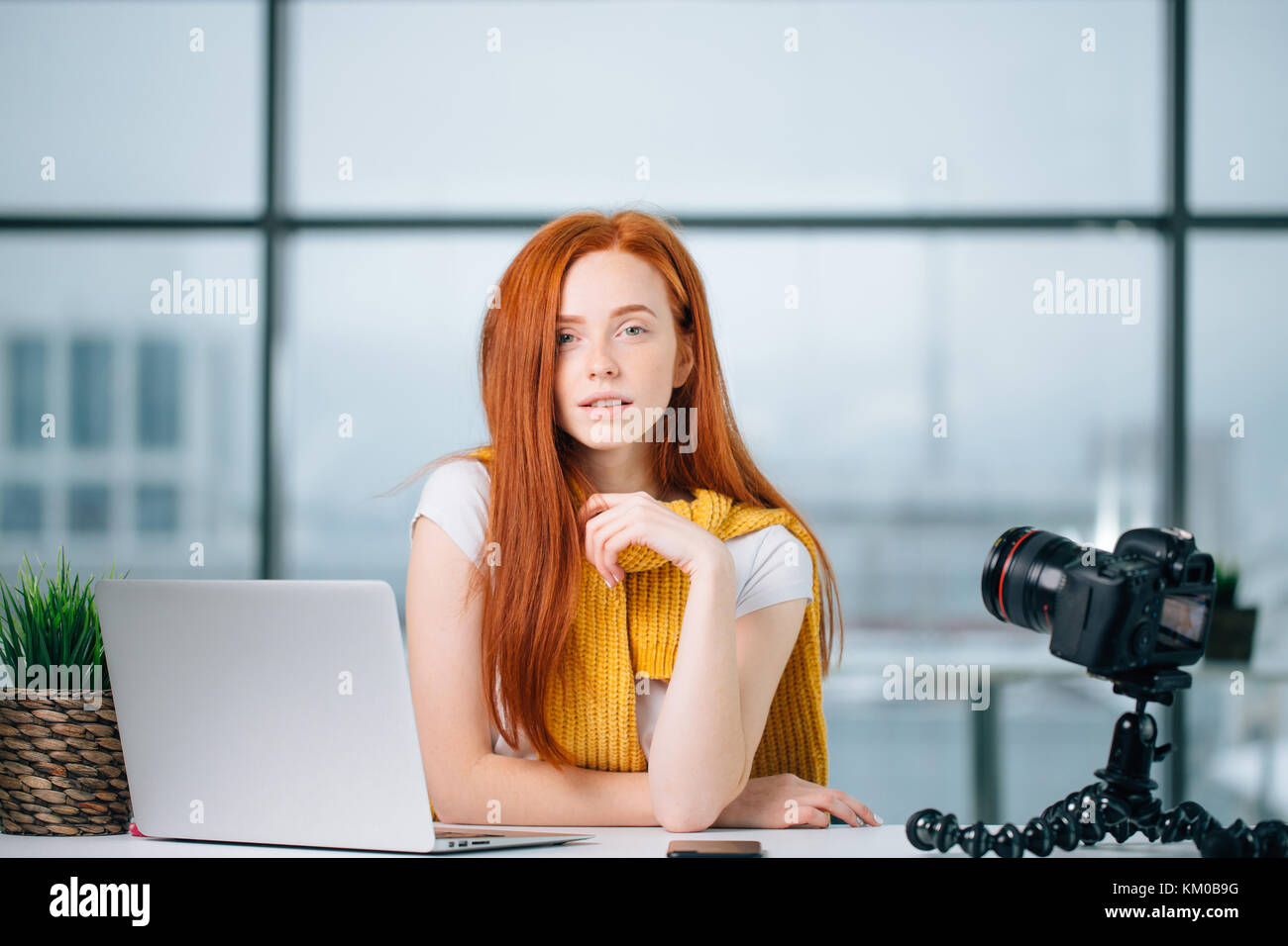 Young female blogger with laptop and book on camera screen looking at ...