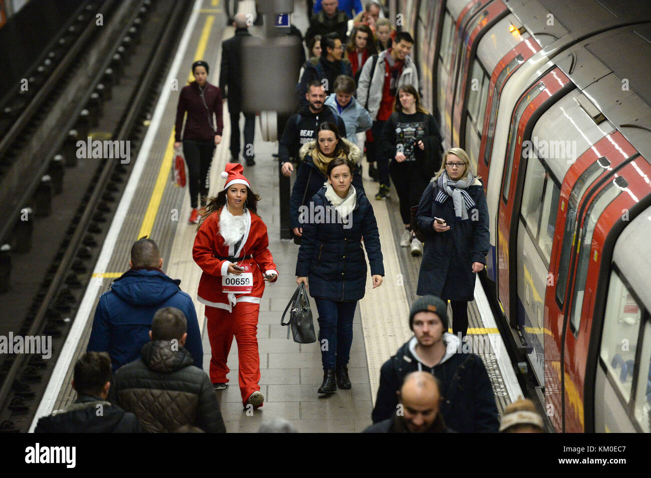 A woman dressed as Santa Claus walks along an underground platform, as ...