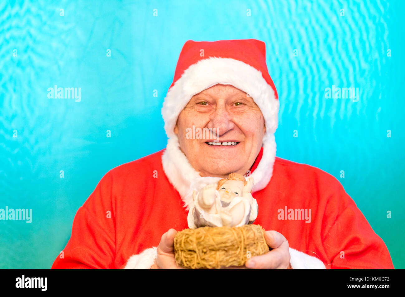 old man wearing Santa Claus costume smiling while holding a statue of ...