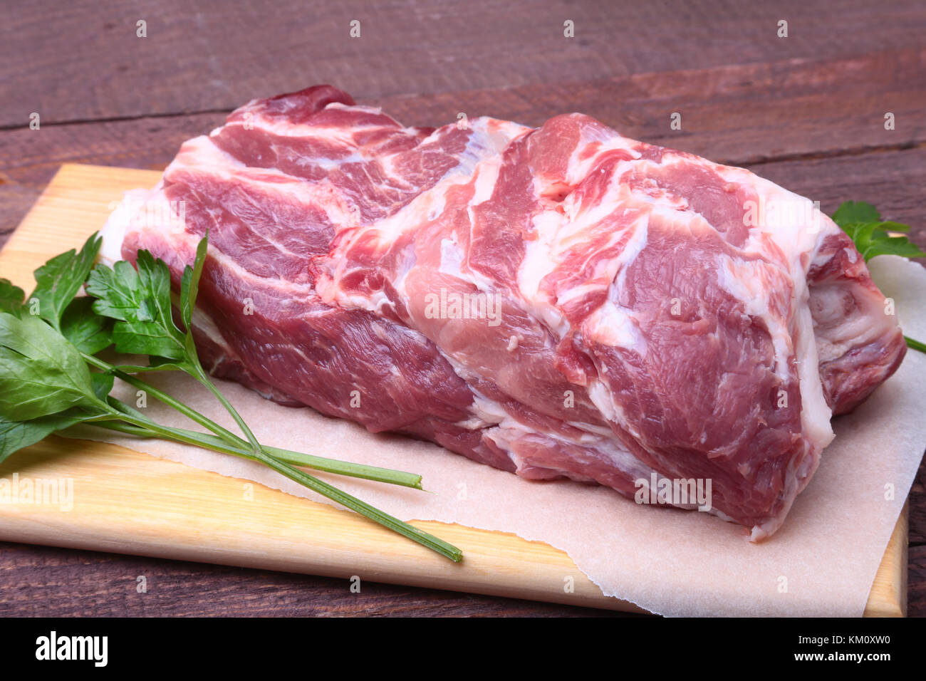 Raw pork neck chop meat with parsley herb leaves on a stone background ...
