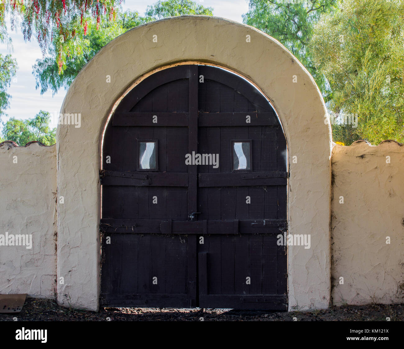 arched adobe wall with brown wooden door outside a California mission ...