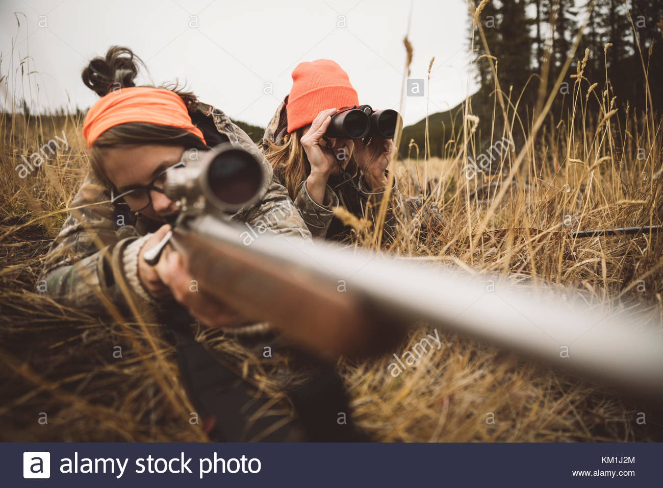 Mother and daughter hunters laying, using binoculars and hunting rifle ...