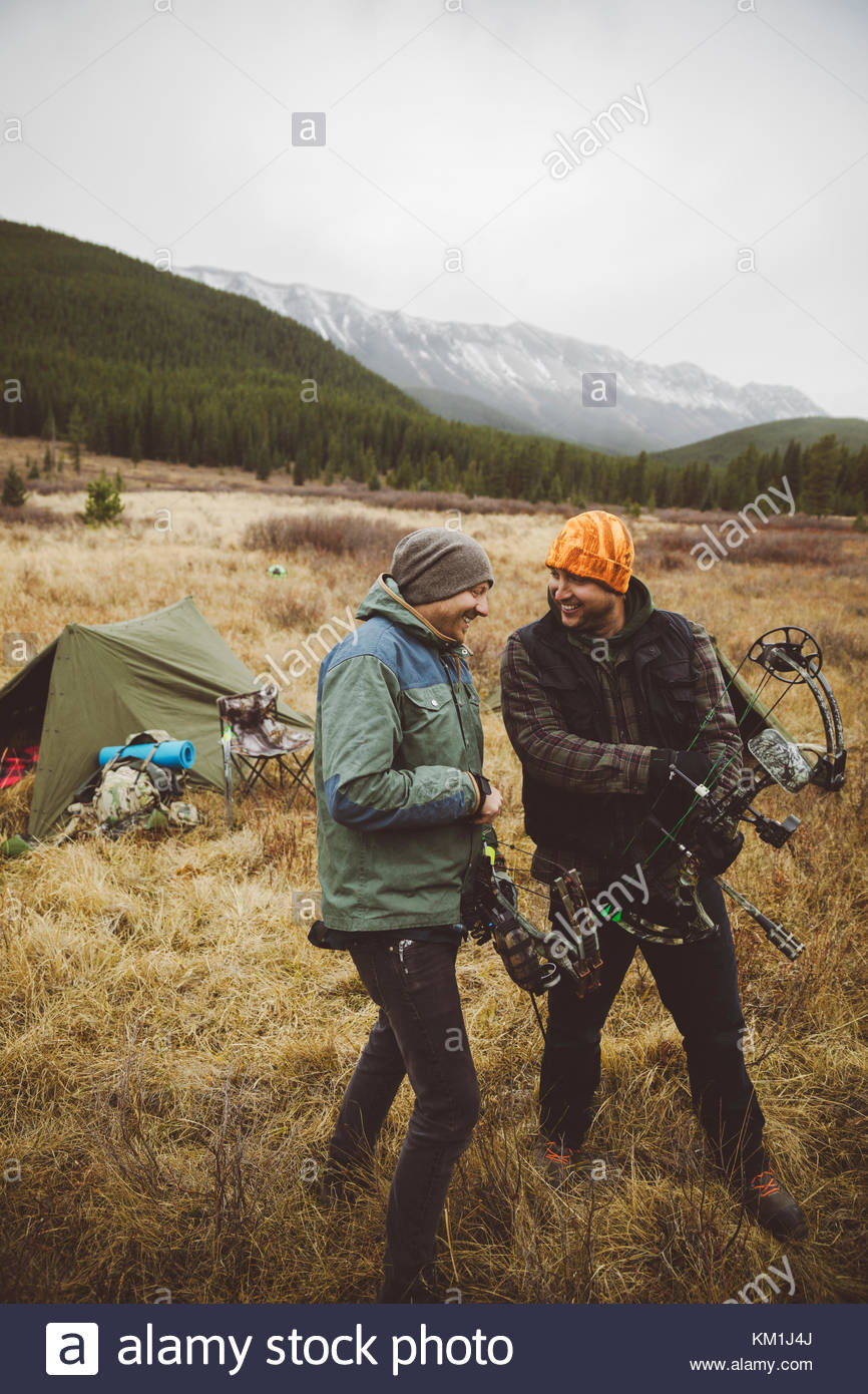 Male hunter friends with hunting compound bows outside tent at campsite ...