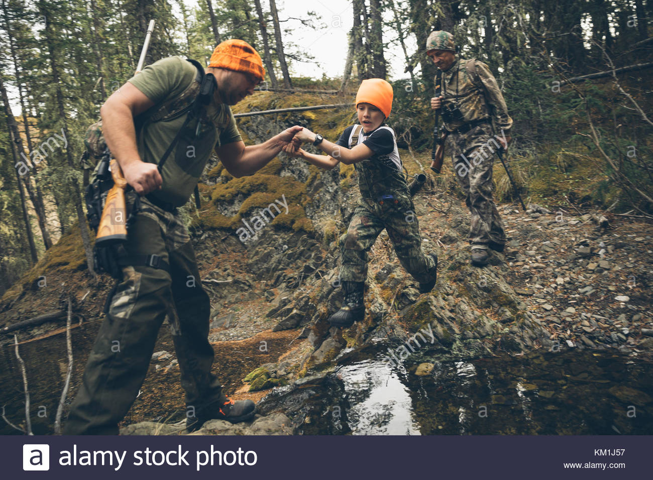 Father hunter helping son crossing rocks in forest Stock Photo - Alamy