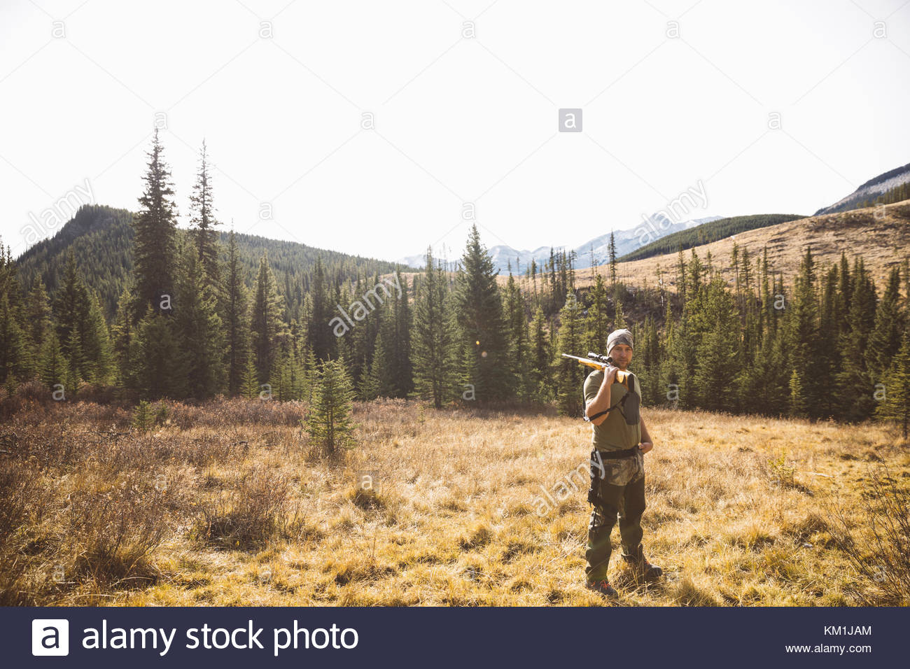 Portrait male hunter holding hunting rifle in sunny, remote field Stock ...
