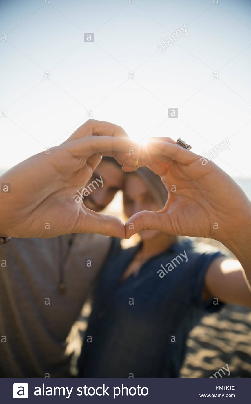 Portrait affectionate couple forming heart-shape with hands on sunny ...