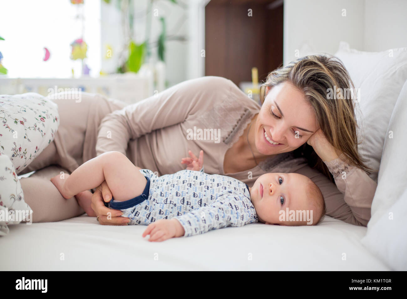 Young mother, lying in bed with her newborn baby boy, playing and ...