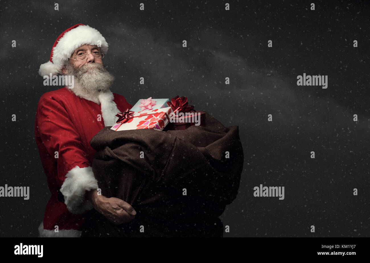 Santa Claus is bringing Christmas gifts in a huge heavy sack, snow ...