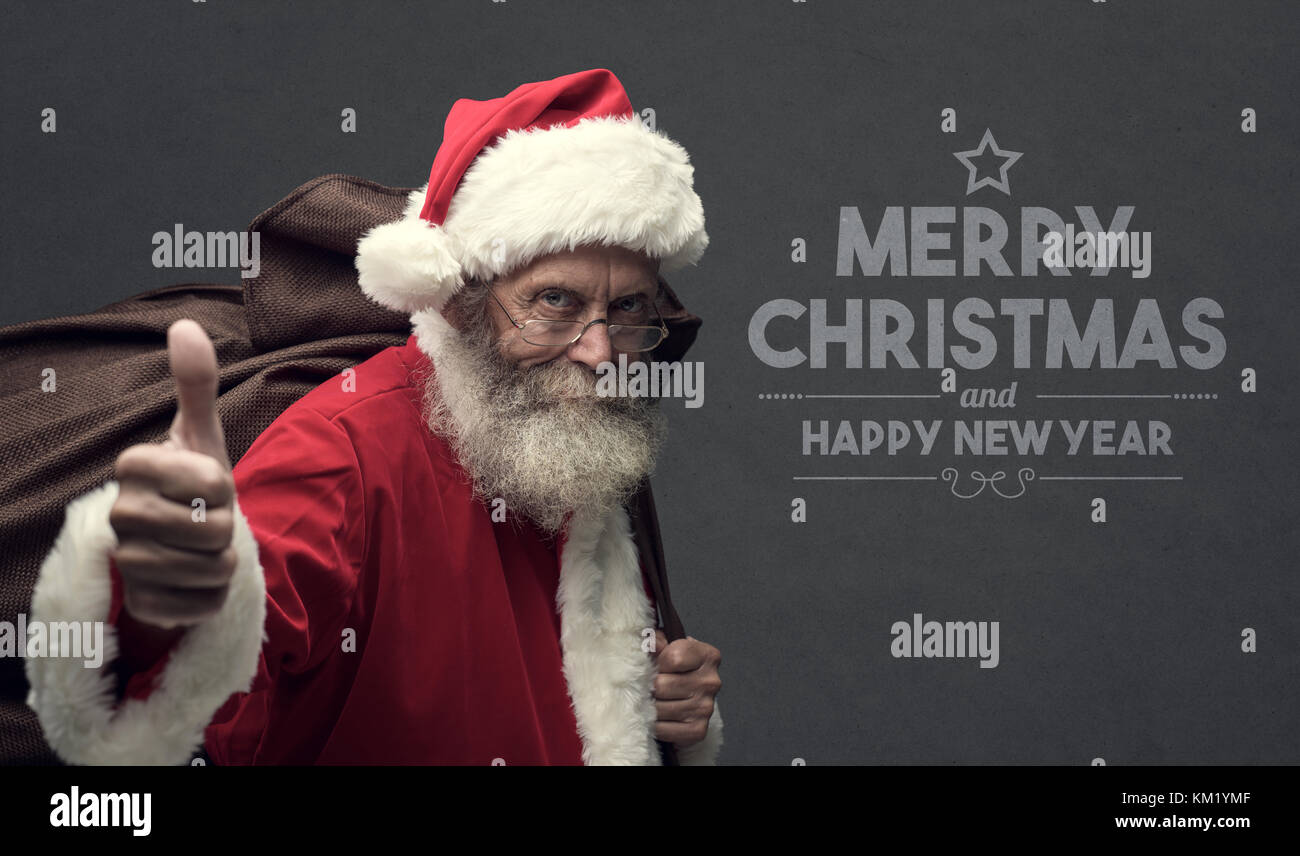 Confident happy Santa Claus giving a thumbs up and carrying Christmas ...