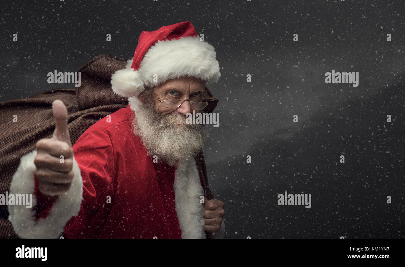 Confident happy Santa Claus under the snow, he is giving a thumbs up ...