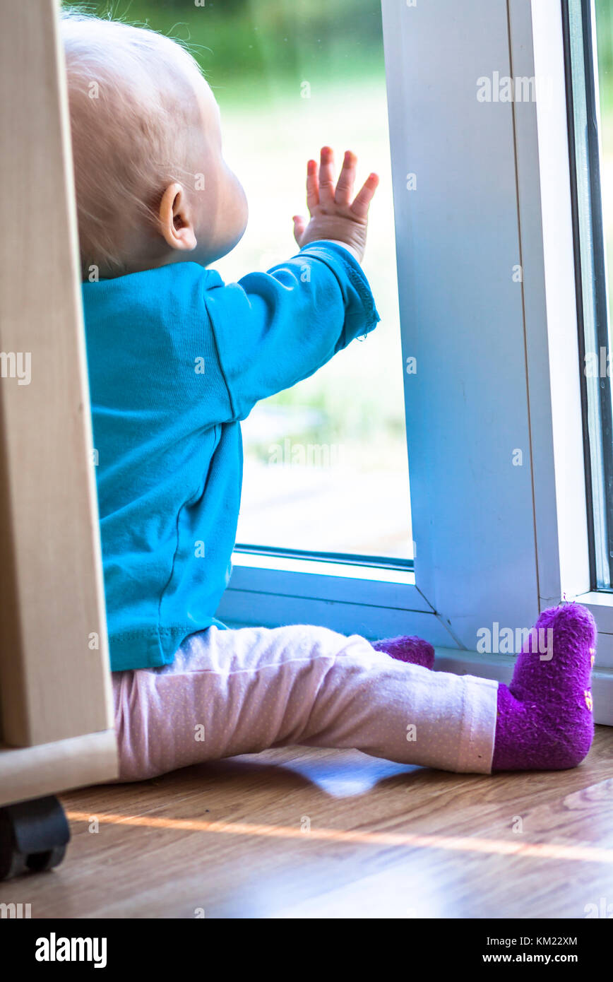 View form behind of toddler sitting in front of a big window with the ...